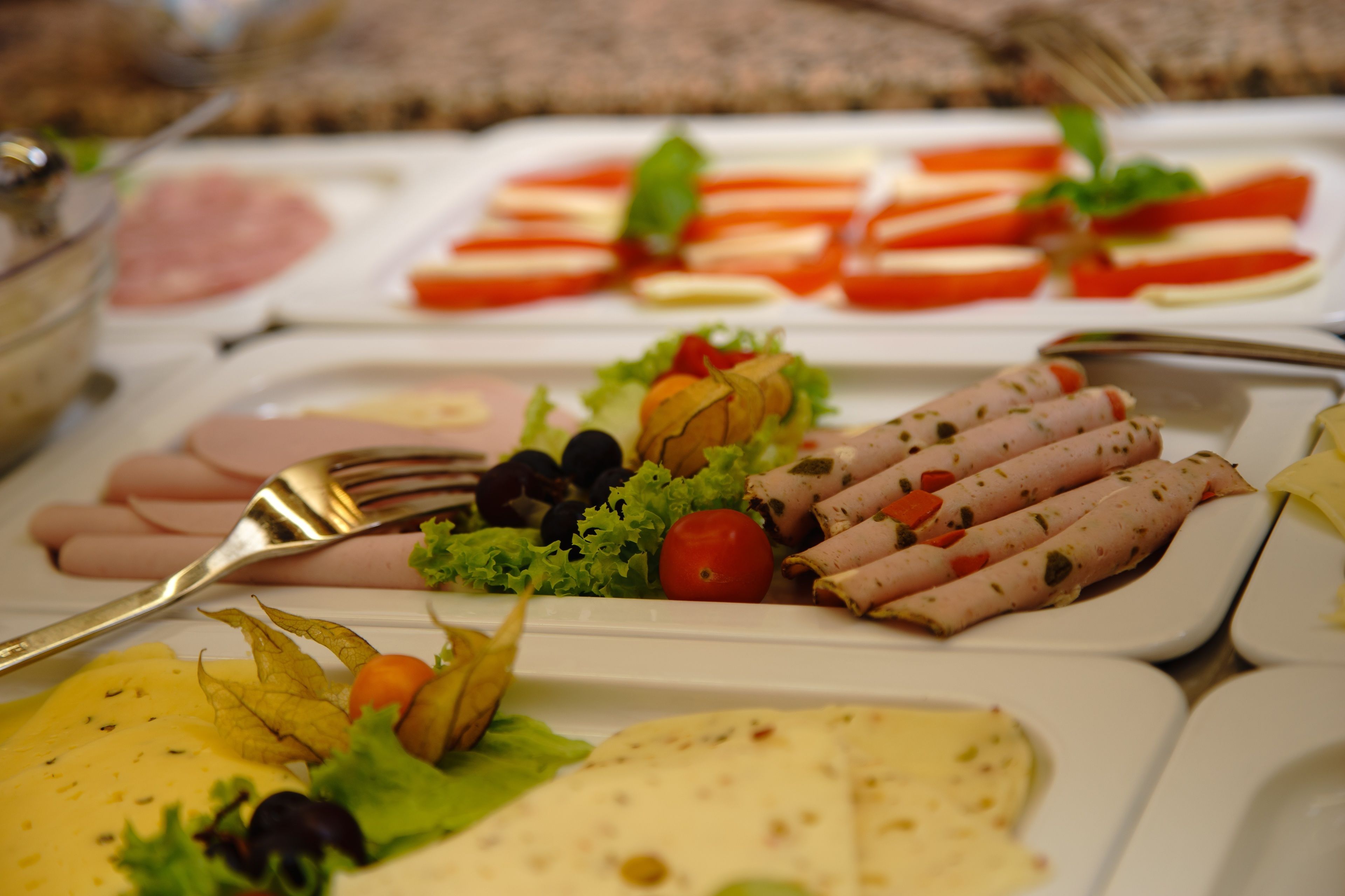 Buffet com diversos alimentos, incluindo tomates fatiados, alface e pães.