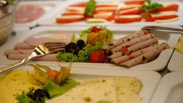 Buffet com diversos alimentos, incluindo tomates fatiados, alface e pães.