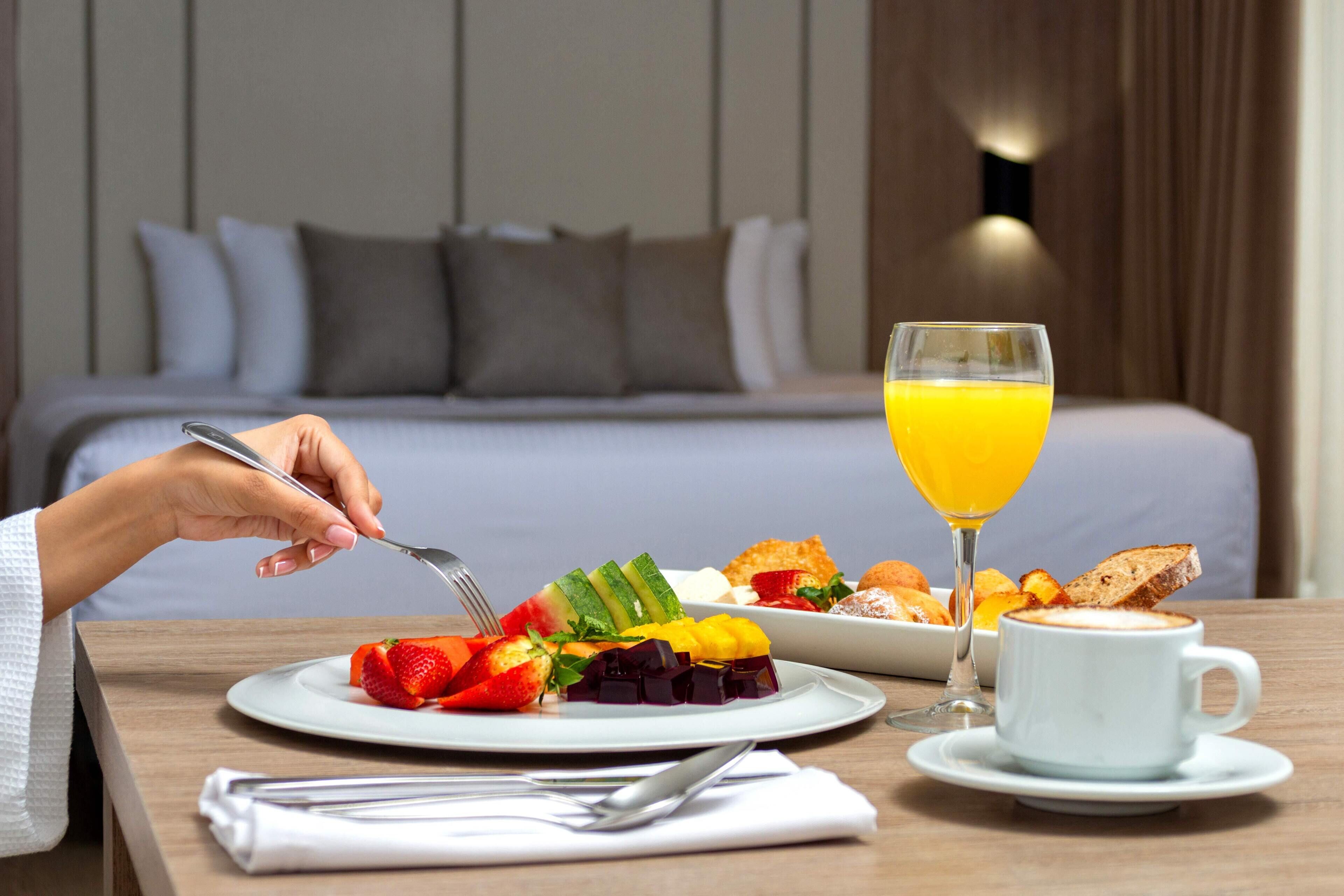 Uma mesa de madeira com um conjunto de café da manhã, incluindo uma tábua de frutas, torradas e um copo de suco de laranja.