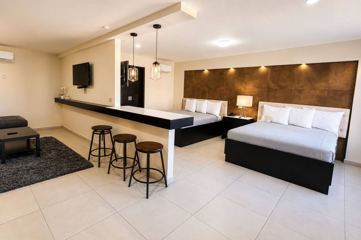 Quarto de hotel moderno com sofá, mesinha, espaço de bar e cama.