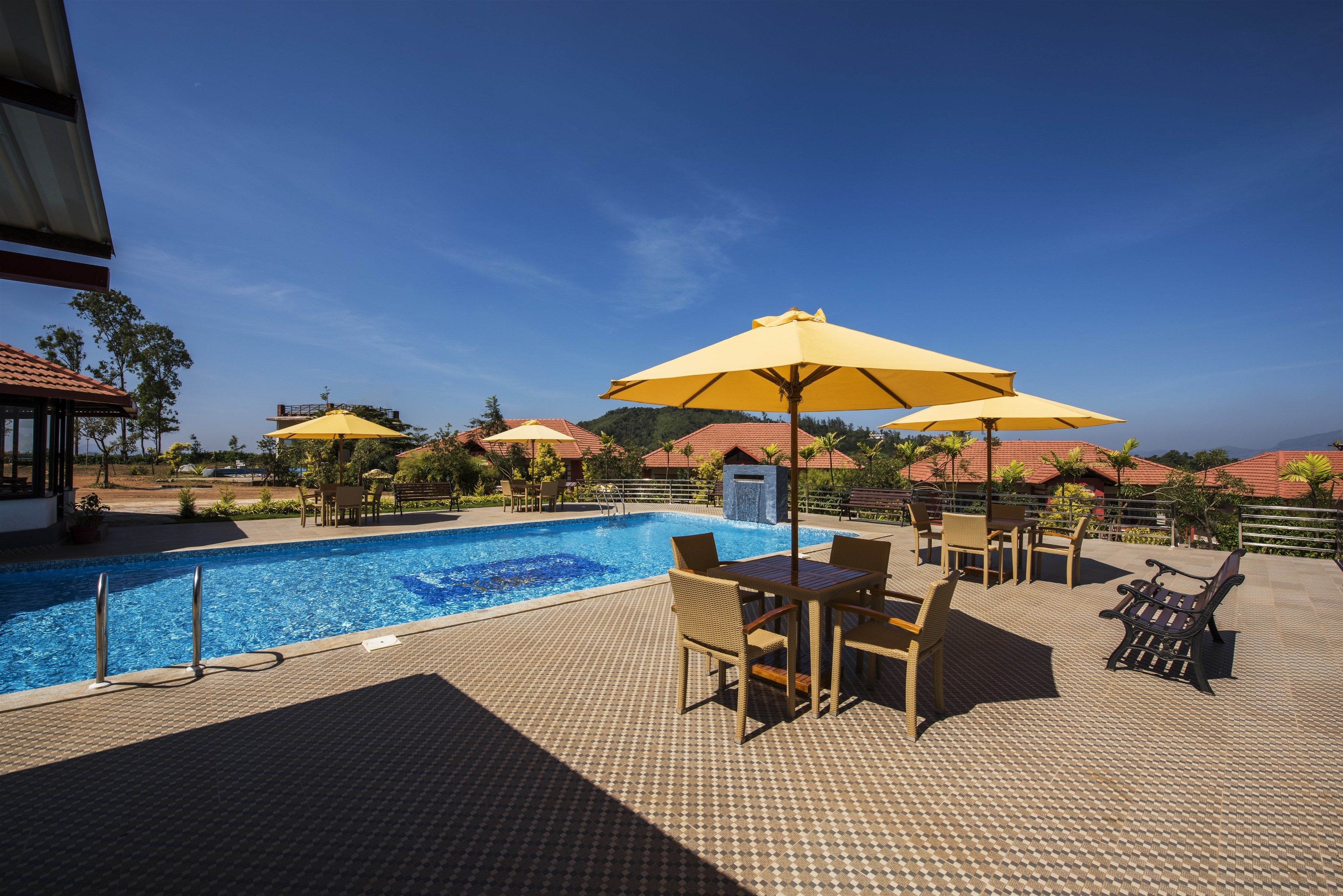 Uma área à beira da piscina com um deck ladrilhado, guarda-sóis amarelos e mobiliário de exterior.