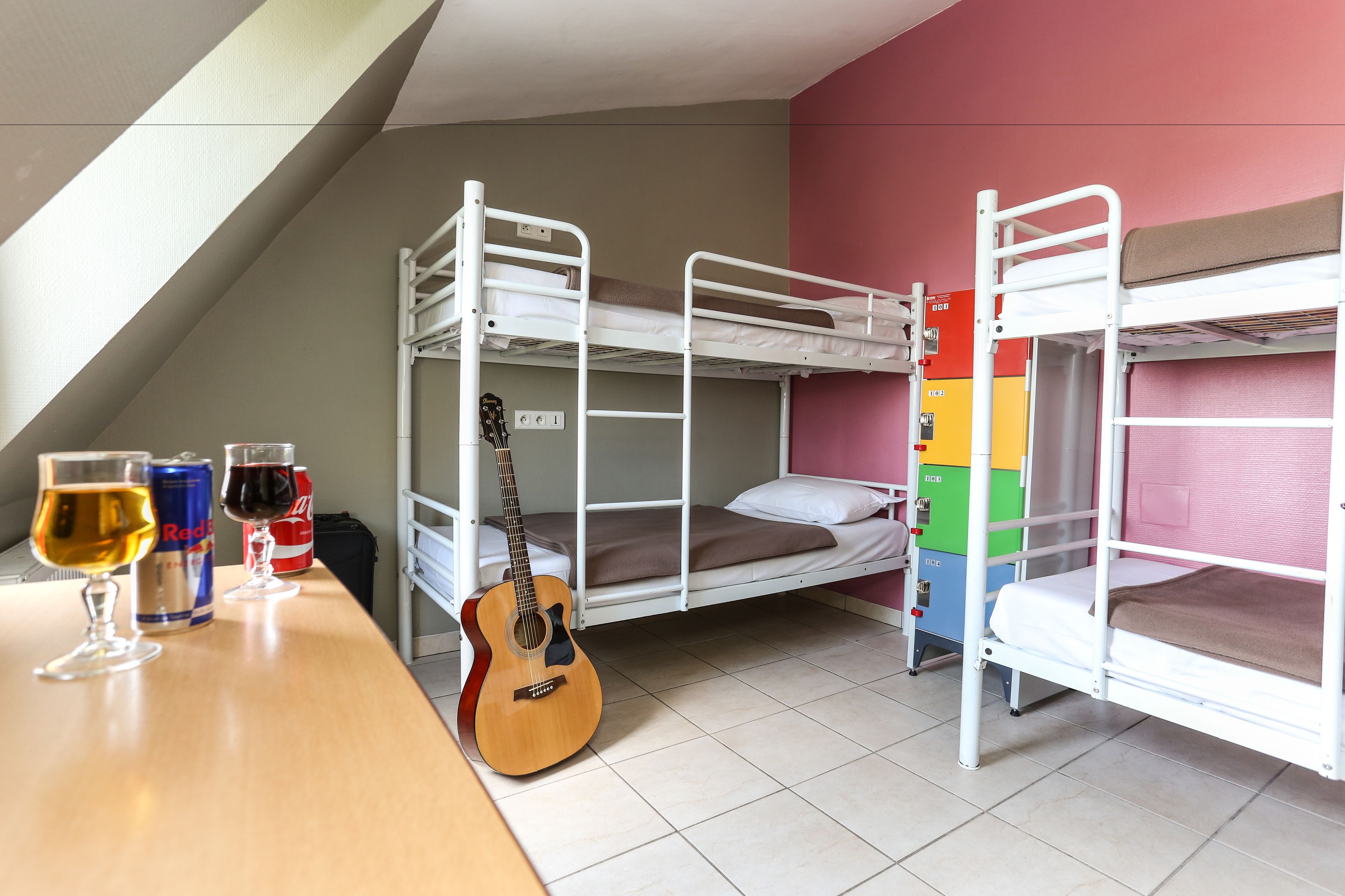 Quarto em dormitório com beliches, um violão e bebidas sobre uma mesa.