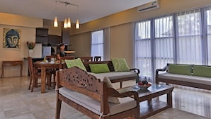 Sala de estar moderna com sofá, mesa de jantar e cadeiras. Há um quadro de Buda na parede e uma janela com cortinas.