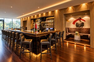 Uma área de bar com balcão extenso, vários bancos e prateleiras cheias de garrafas.