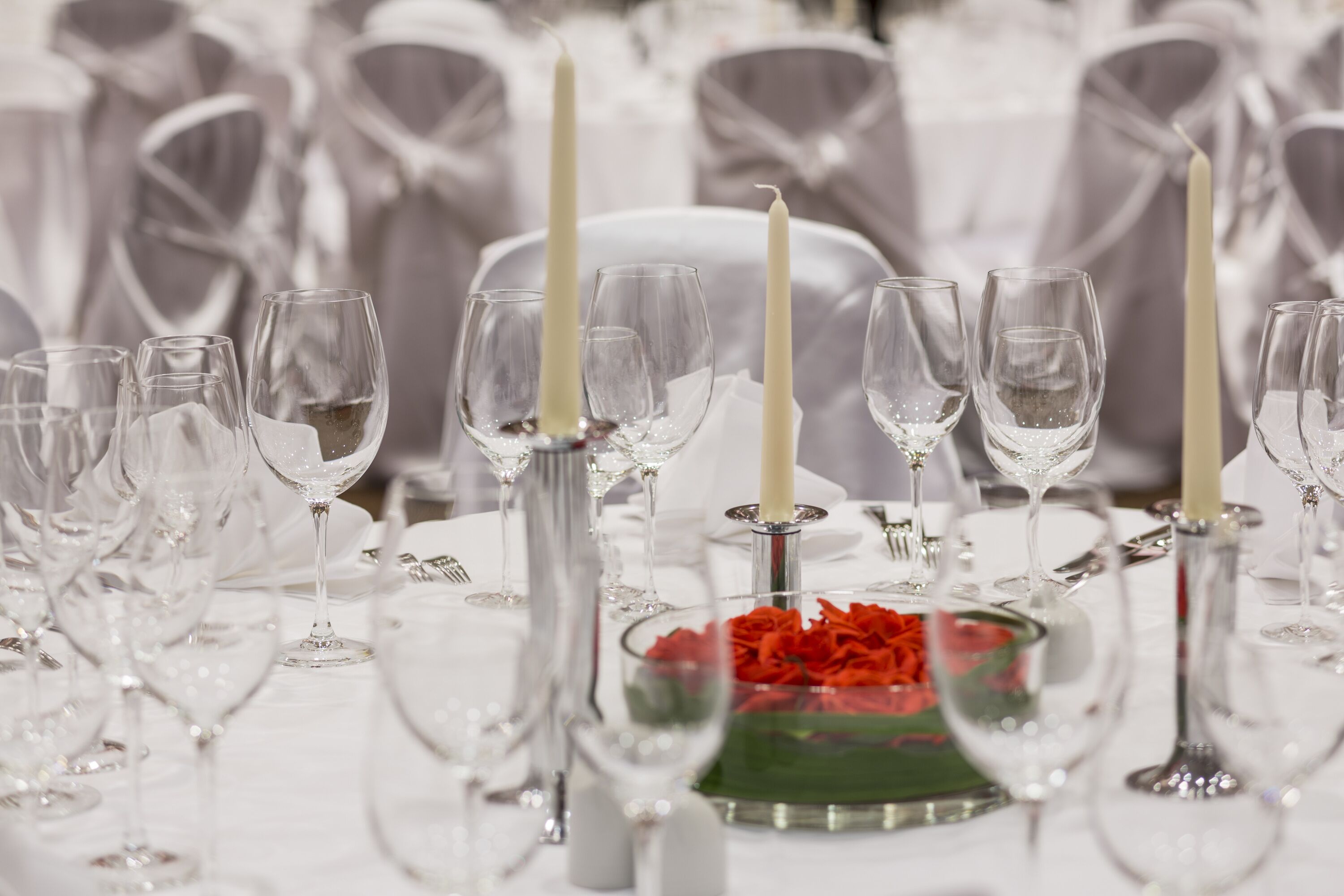 Mesa posta para um evento formal, com vários copos de vinho e velas.