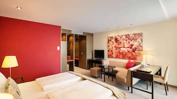 Quarto de hotel com uma cama, uma escrivaninha com cadeira, uma televisão e uma grande obra de arte floral na parede.