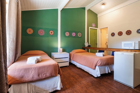Quarto com duas camas, um refrigerador branco pequeno, mesa de cabeceira com abajur e pratos decorativos na parede.