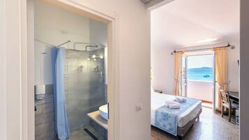 Quarto de hotel com banheiro que inclui box de vidro e varanda com vista para o mar.