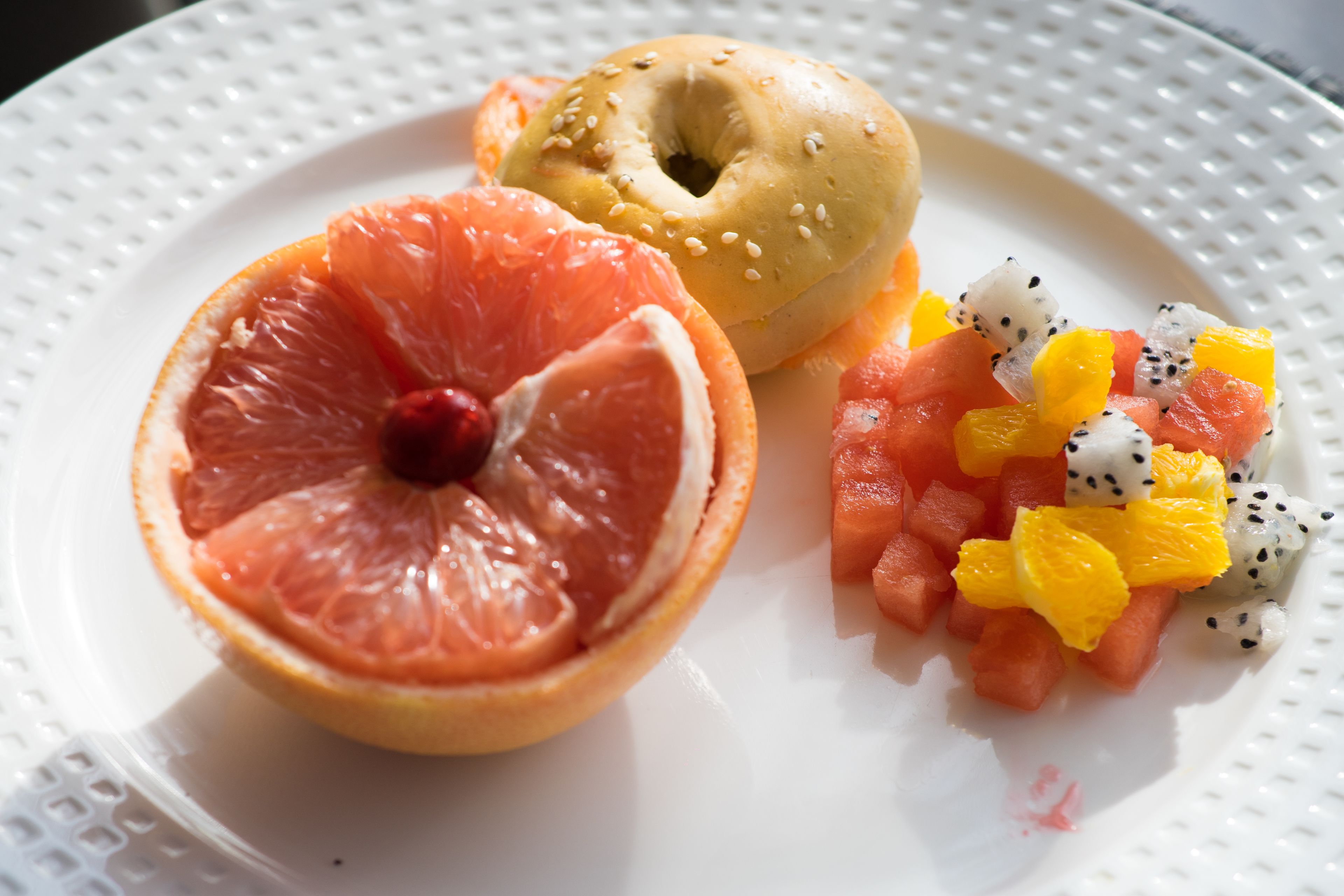 Um prato com meia toranja, um bagel e uma salada de frutas.