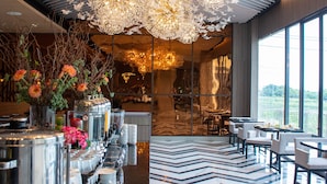 Decoração moderna com um lustre central, área de bar com bebidas e vista através de grandes janelas.