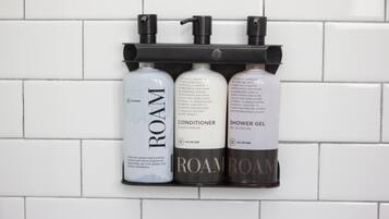 Três frascos de condicionador e gel de banho Roam sobre uma parede de azulejos brancos.