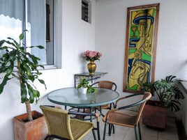 Uma mesa de vidro redonda com cadeiras de vime, uma planta em vaso e um vaso com flores.
