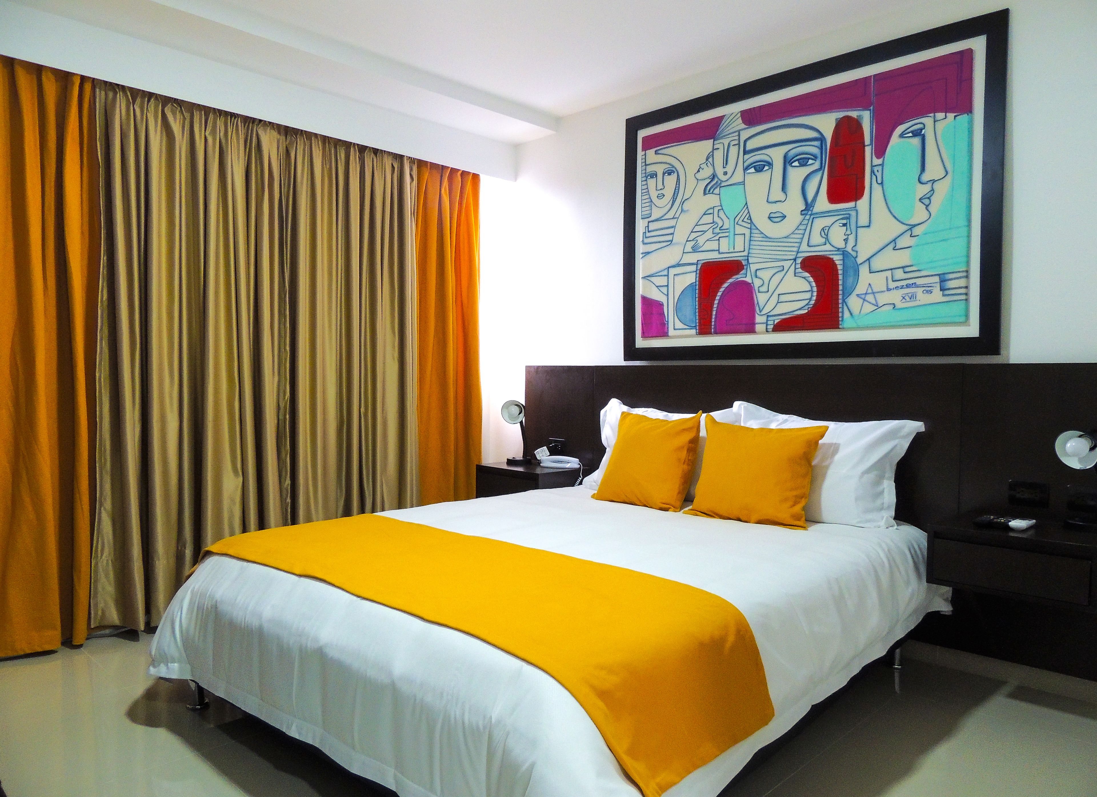 Quarto de hotel com uma cama grande, mesa de cabeceira, espelho e um quadro na parede.