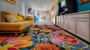 Uma sala de estar vibrante com um tapete floral colorido, um sofá com almofadas estampadas e uma TV sobre um móvel.