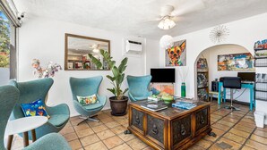 Uma sala de estar com cadeiras cor de verde-água, uma mesa de centro de madeira, um vaso com planta e uma televisão.