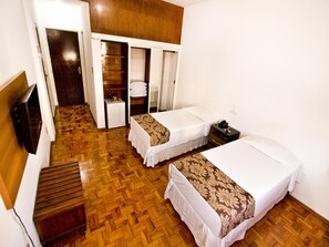 Quarto de hotel com duas camas, chão de madeira, televisão, guarda-roupa e uma pequena mesa.