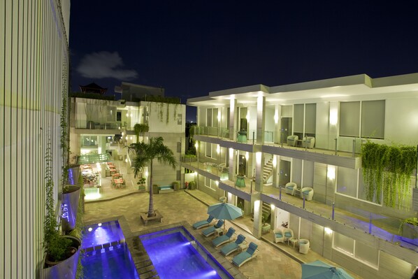 Um hotel com vários andares, piscina no terraço, área de estar externa e interior bem iluminado.