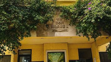 Um edifício amarelo com uma placa indicando 'HOTEL DON MIGUEL' e um mural retratando uma cena de rua.