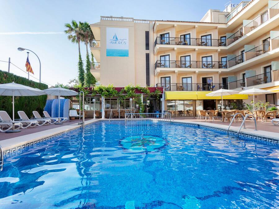 Área de piscina de hotel com espreguiçadeiras, guarda-sóis e um edifício com varandas.