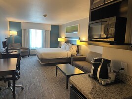 Quarto de hotel com cama, secretária, sofá, máquina de café e micro-ondas.