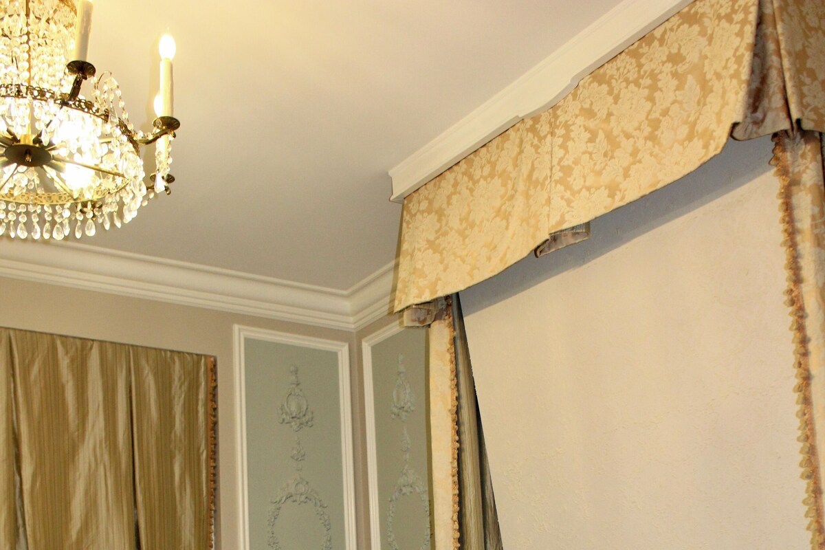 Quarto com cama, cortinas, lustre e espelho.