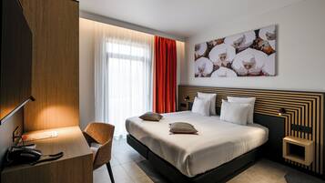 Quarto de hotel moderno com uma cama grande, uma escrivaninha com telefone, uma cadeira e uma obra de arte na parede.