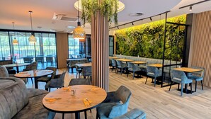 Um restaurante moderno com mesas redondas, cadeiras azuis e uma parede verde com plantas.