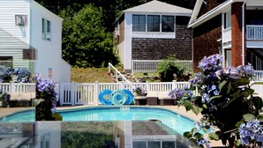 Piscina com cerca branca, duas casas e uma árvore ao fundo.