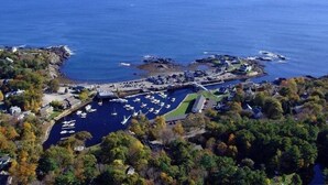 Vista aérea de uma marina costeira com barcos atracados, cercada por edifícios residenciais e vegetação densa.