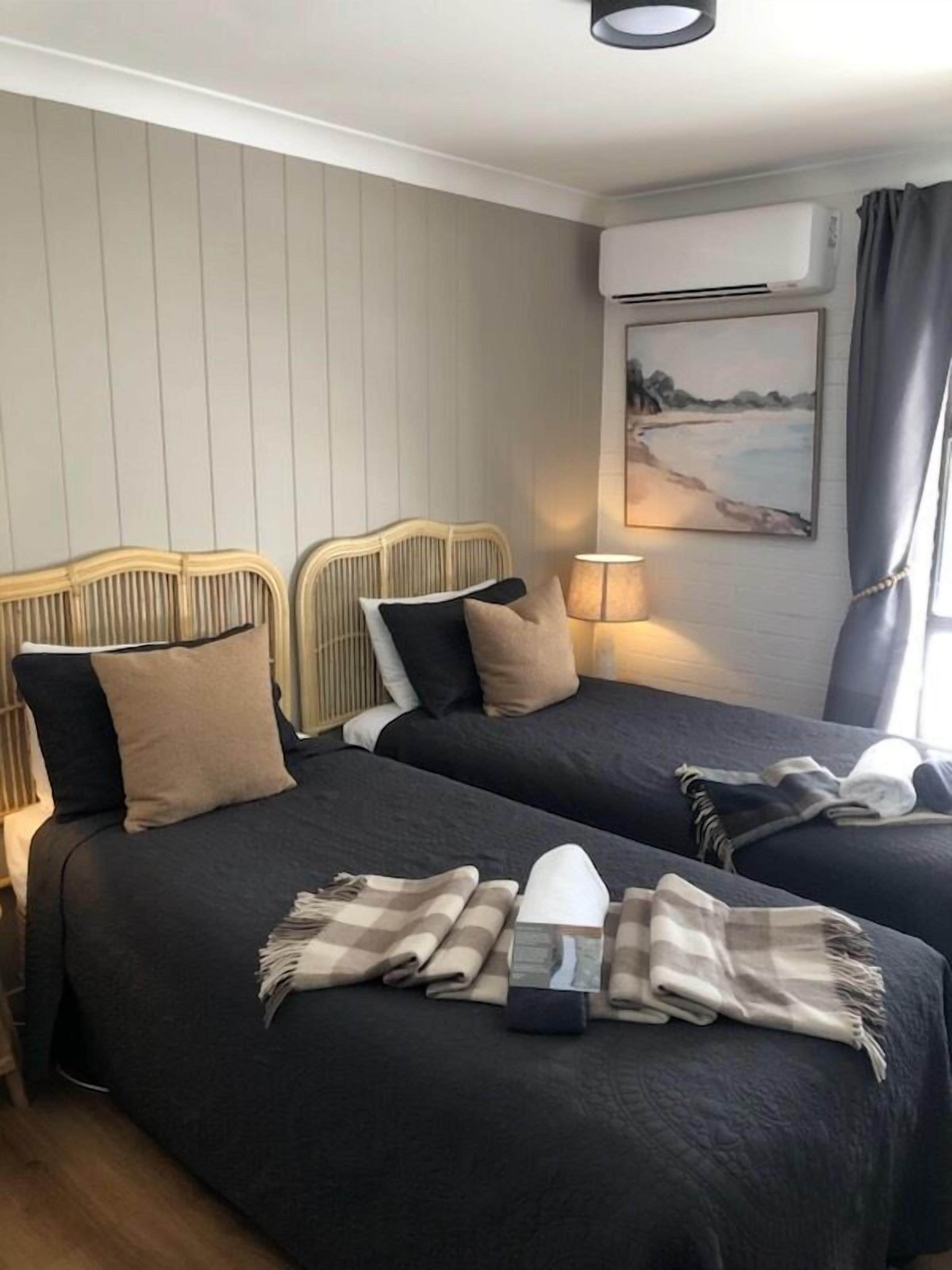 Quarto de hotel com duas camas, um quadro na parede e uma janela com cortinas.