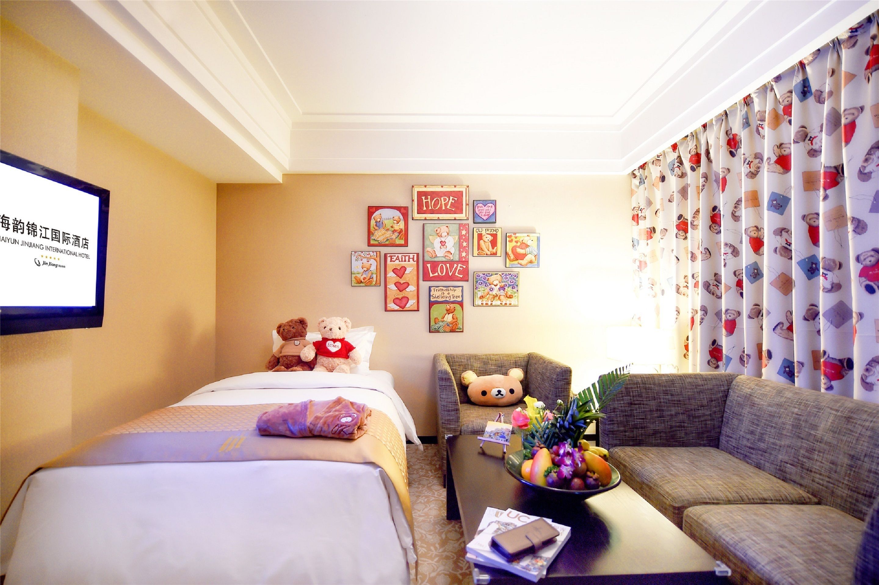 Quarto de hotel com cama, sofá, mesa de centro com um cesto de frutas e parede com quadros.