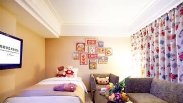Quarto de hotel com cama, sofá, mesa de centro com um cesto de frutas e parede com quadros.