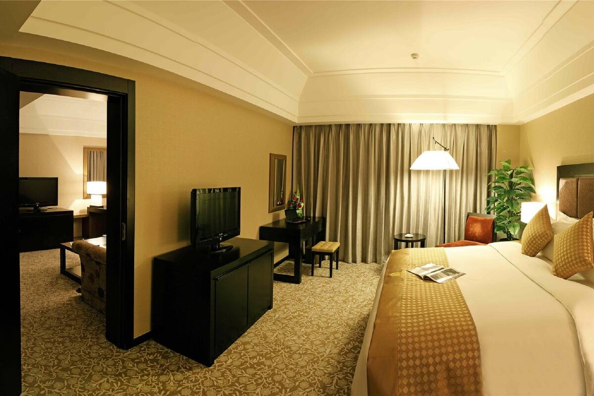 Quarto de hotel com cama, mesa de cabeceira, televisão, escrivaninha, cadeira e cortinas.