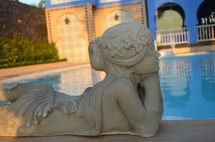 Escultura de pedra de uma sereia perto de uma piscina.