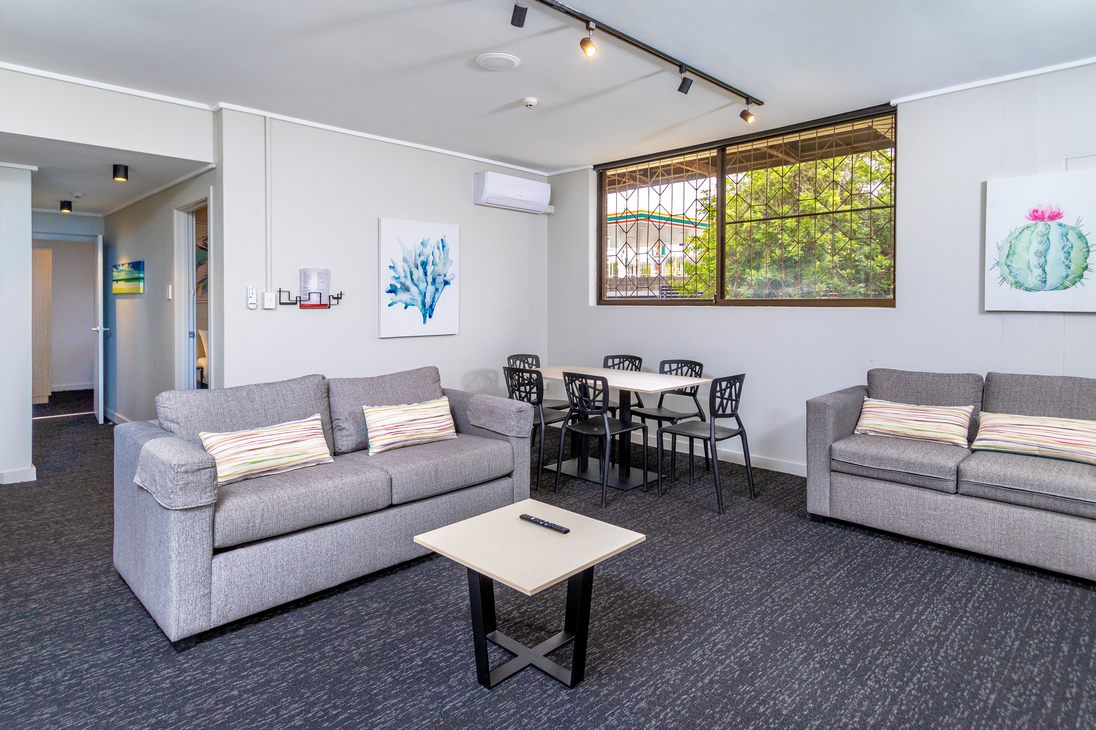 Quarto moderno com dois sofás cinzentos, uma mesa pequena e uma área de jantar com cadeiras.