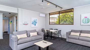 Quarto moderno com dois sofás cinzentos, uma mesa pequena e uma área de jantar com cadeiras.