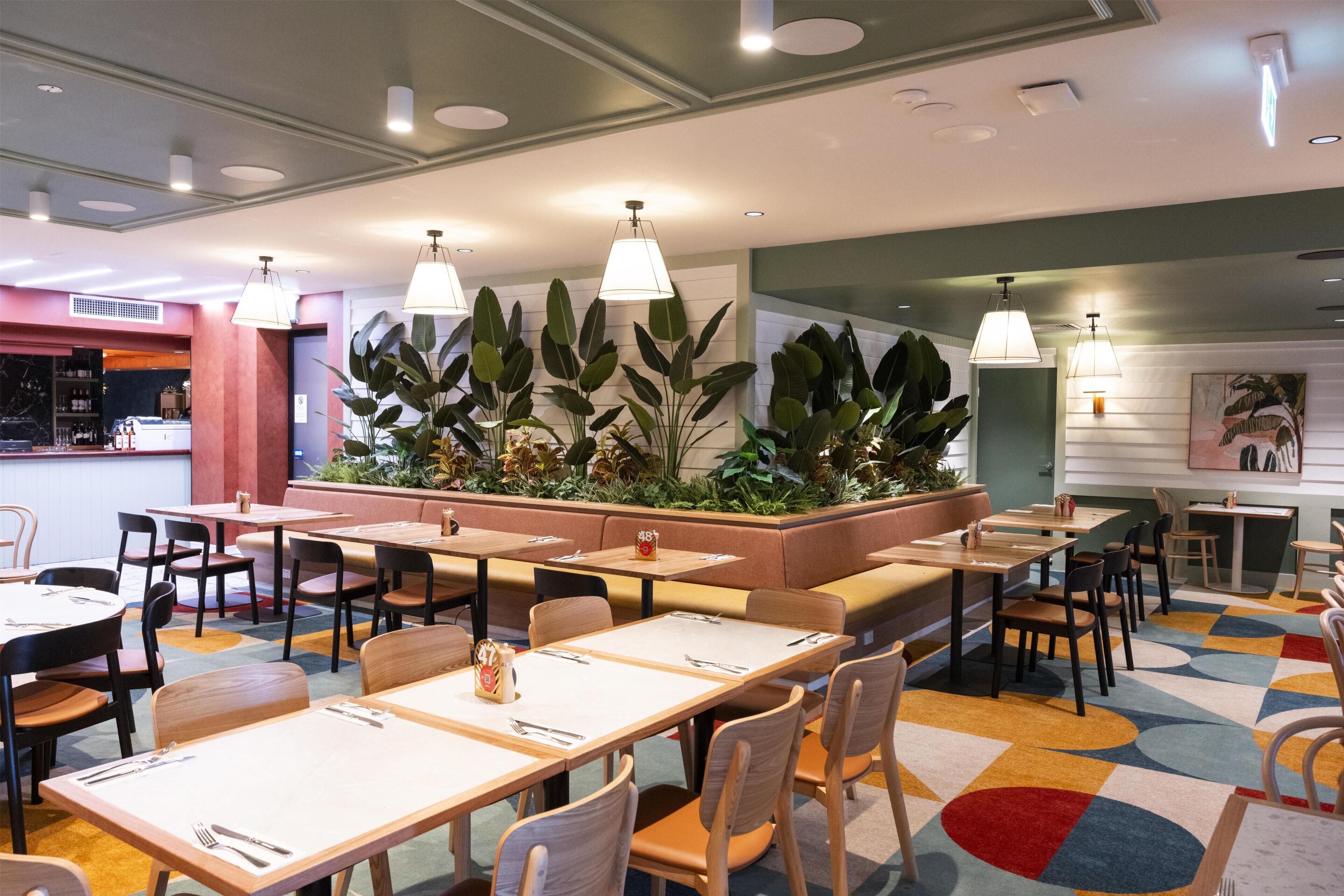 Interior de restaurante com cabines, mesas e plantas penduradas.