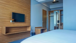 Quarto de hotel moderno com uma cama grande, uma TV fixada numa parede revestida de madeira, uma mesa de cabeceira de madeira, um armário com espelho e um tapete azul.