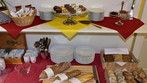 Uma mesa de buffet com diversos pães, doces e um suporte para bolos com sobremesas.