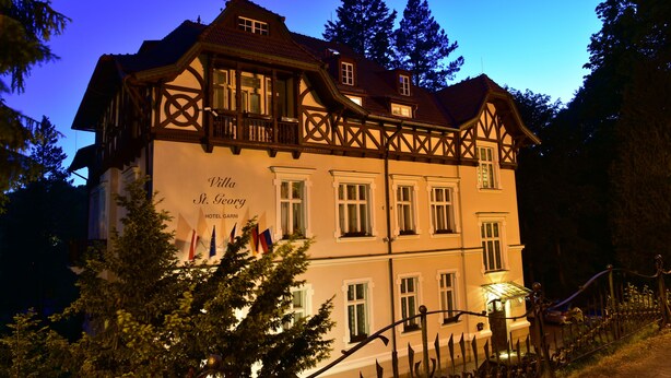 Um hotel europeu tradicional com uma varanda destacada, diversas janelas e uma placa indicando o nome e a localização.
