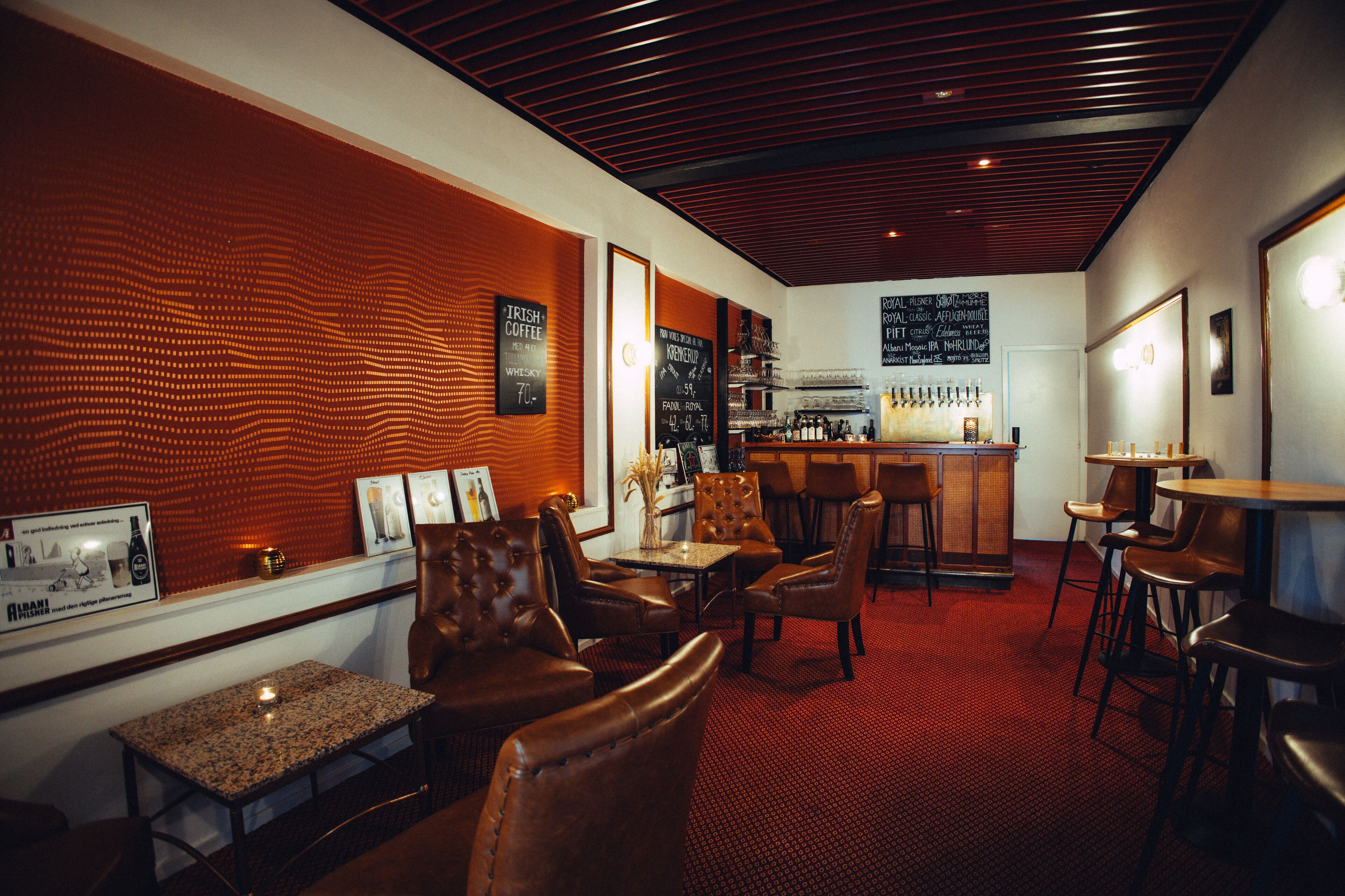 Um espaço de bar acolhedor com assentos de couro, balcão e piso coberto por um tapete vermelho.