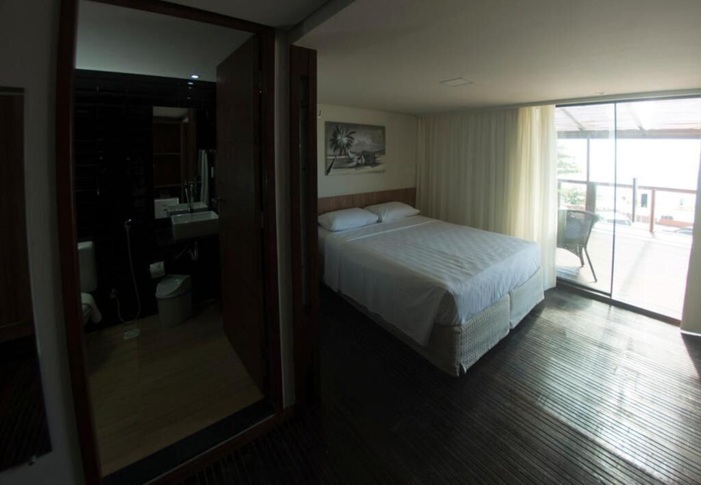 Quarto de hotel com uma cama grande, banheiro com espelho e varanda com vista.