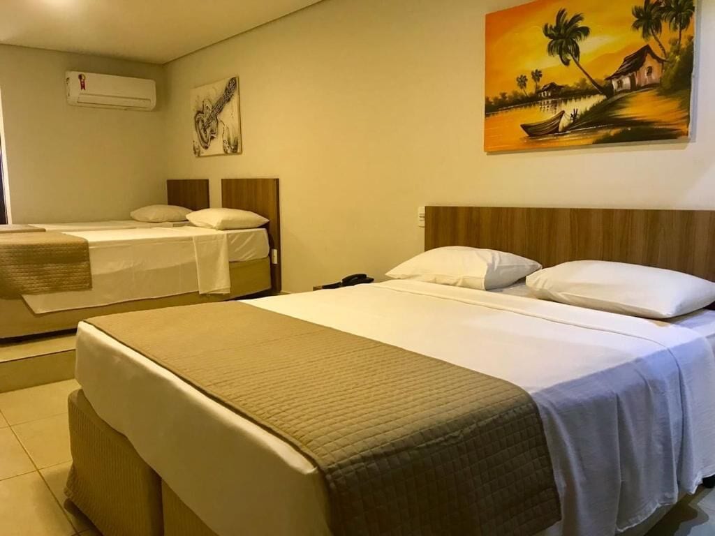 Quarto de hotel com duas camas, um quadro de um pôr do sol e um ar condicionado na parede.