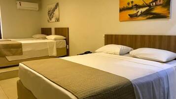 Quarto de hotel com duas camas, um quadro de um pôr do sol e um ar condicionado na parede.