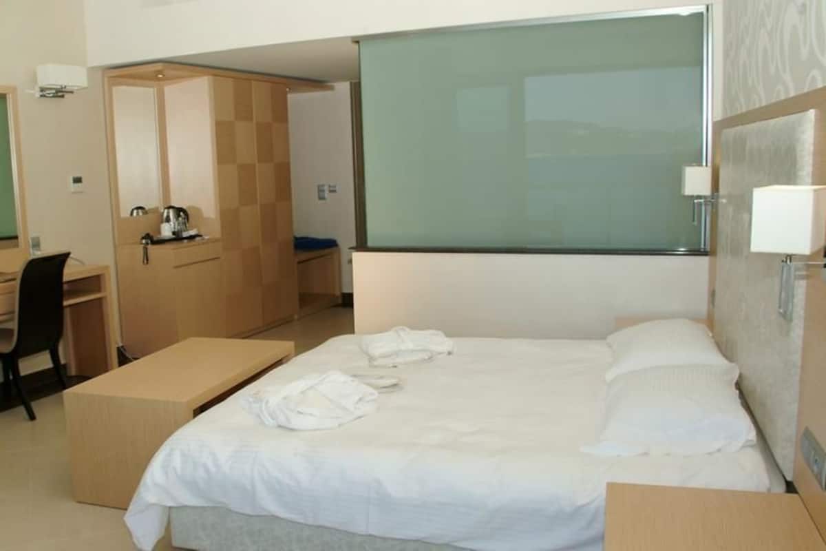 Quarto de hotel com cama, escrivaninha, cadeira, televisão e guarda-roupa.