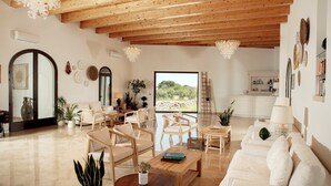 Uma sala de estar espaçosa, com vigas de madeira, um sofá branco e vista para o exterior.