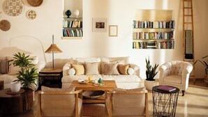 Uma sala de estar acolhedora com sofá, mesa de centro e cadeiras, cercada por estantes de livros e pratos decorativos.