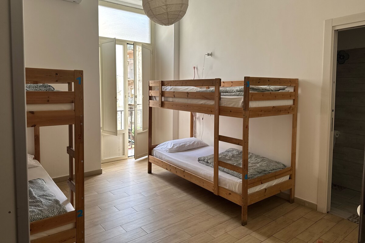 Quarto com duas beliches, janela com vista para a rua e luminária pendente.