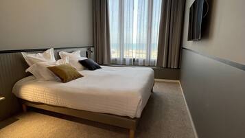 Quarto de hotel moderno com uma cama grande, televisão de tela plana e vista para o mar pela janela.