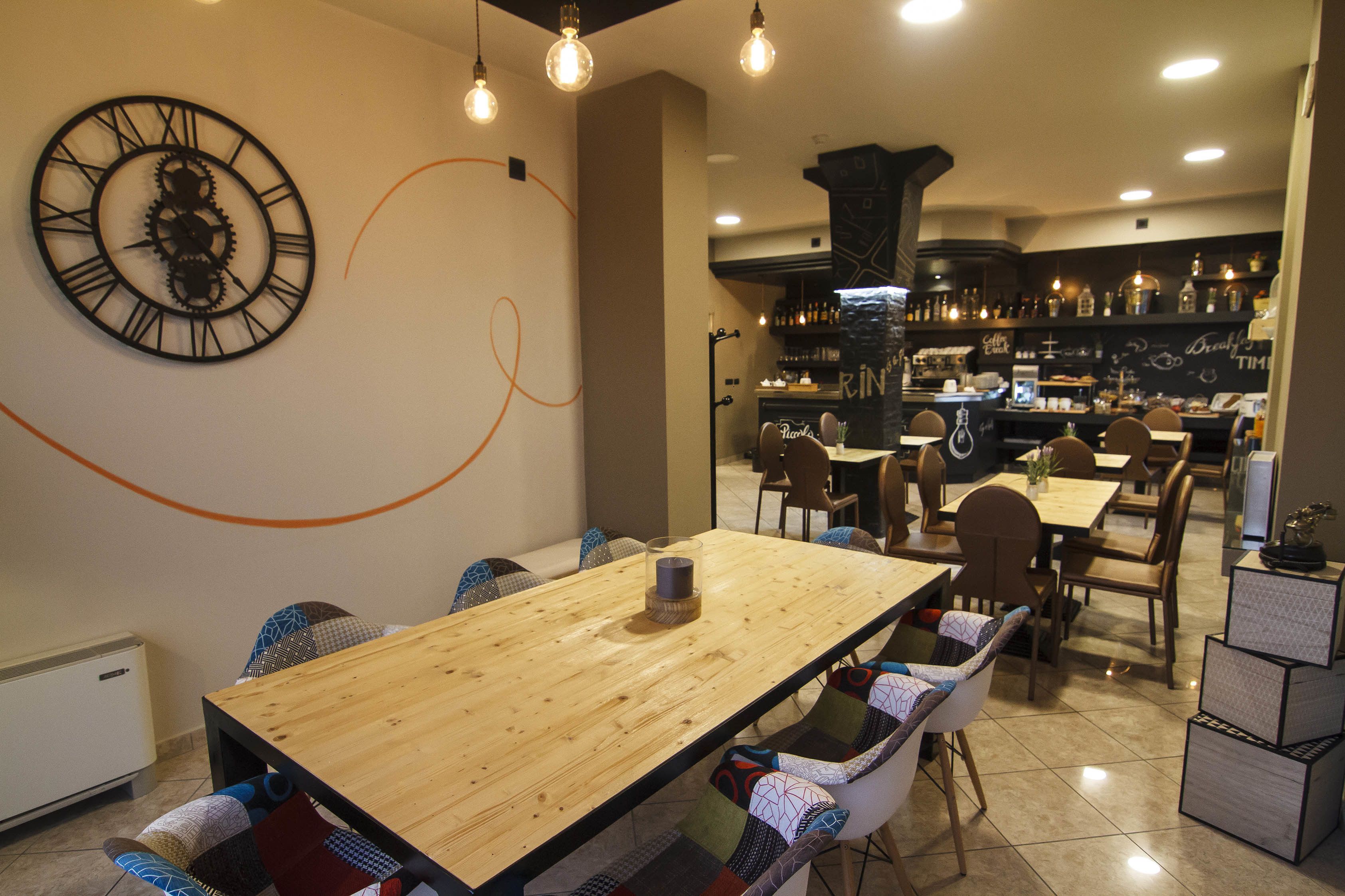 Um restaurante com mesa e cadeiras de madeira, um relógio de parede grande e um balcão ao fundo.